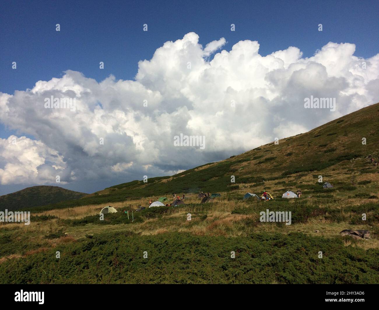 Hikers tenting in green fields and mountains on a blue cloudy sky ...