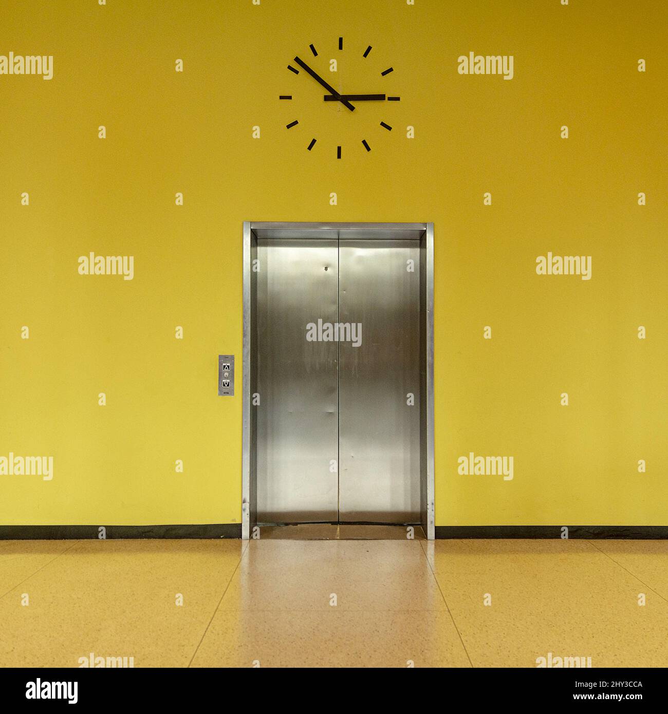 Silver elevator door with the clock above in building with yellow walls ...