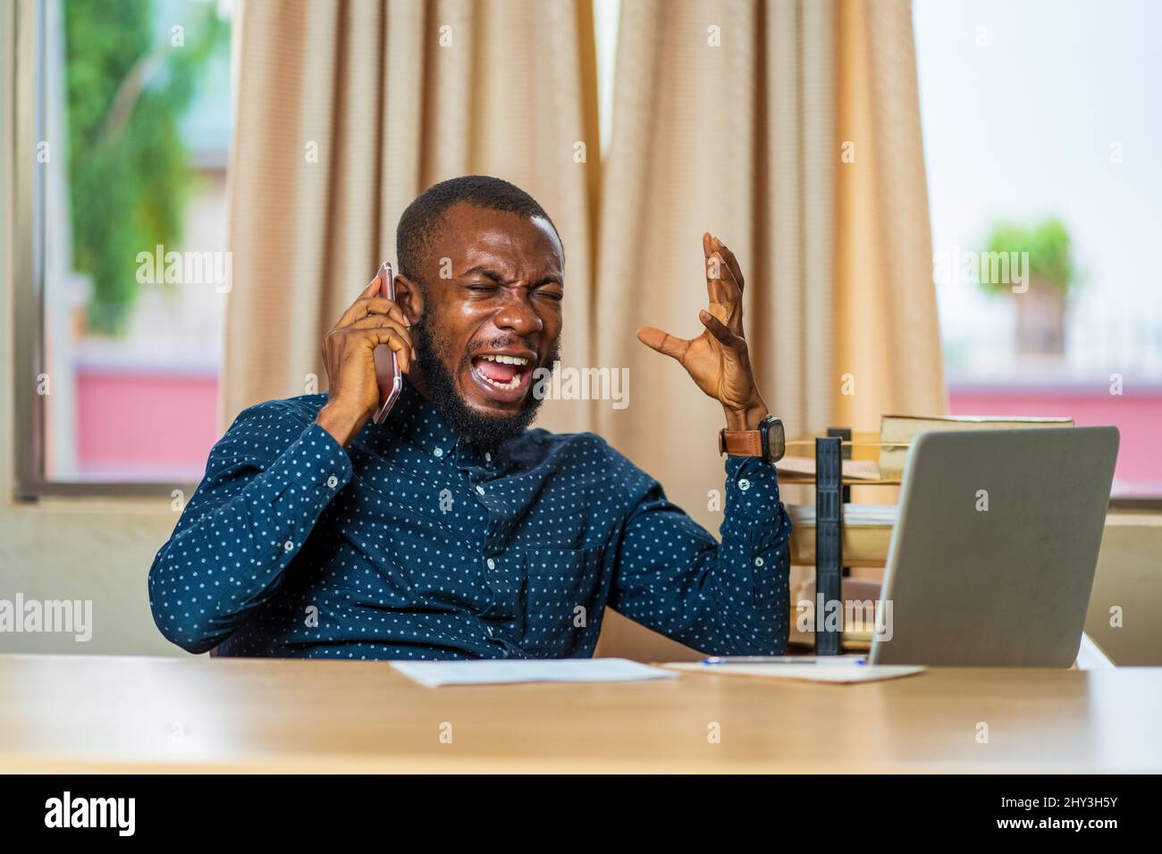 Young Black guy from Ghana working on his desk screaming angrily ...