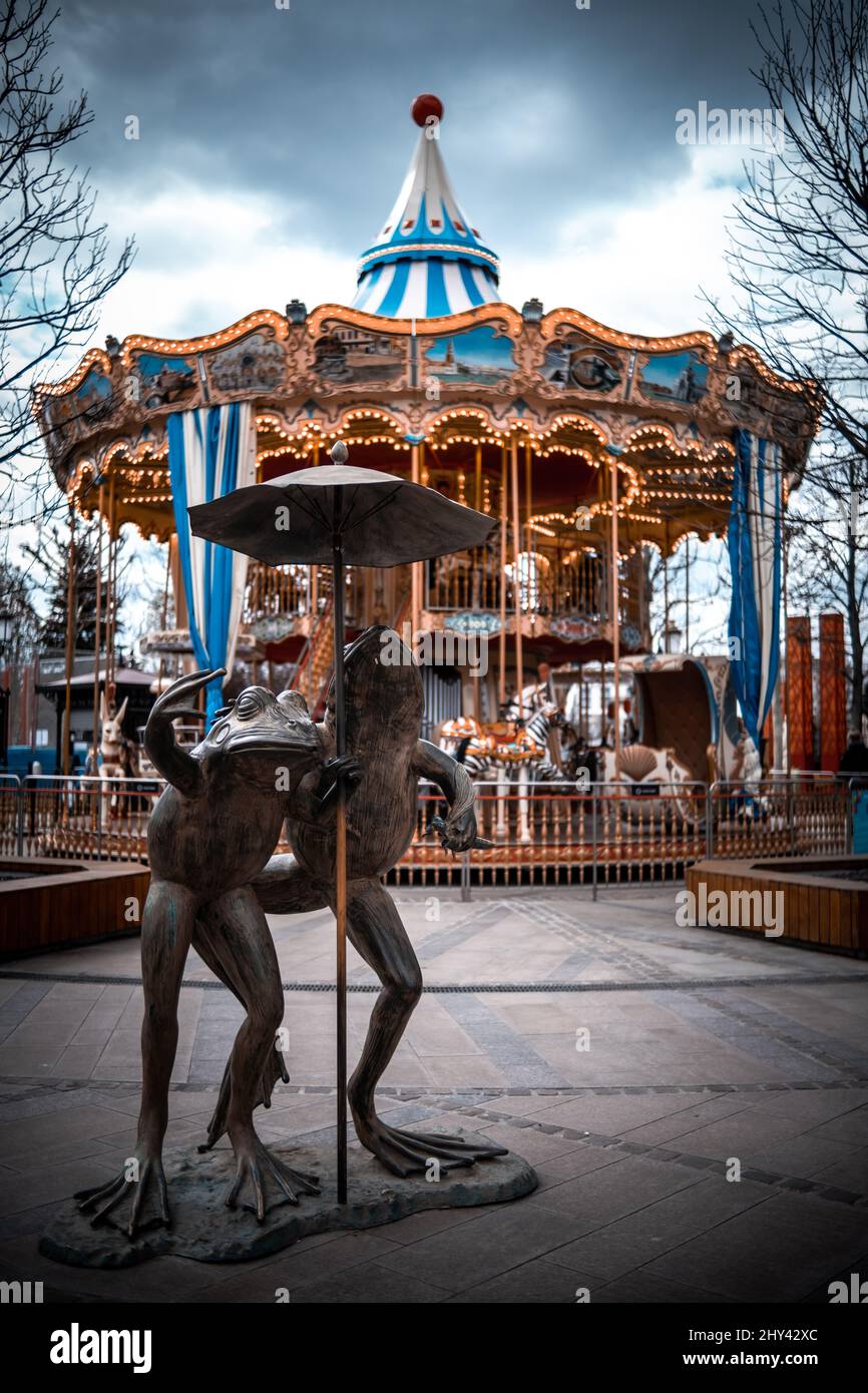 Funny sculpture of frogs in front of a carousel at an amusement park in ...