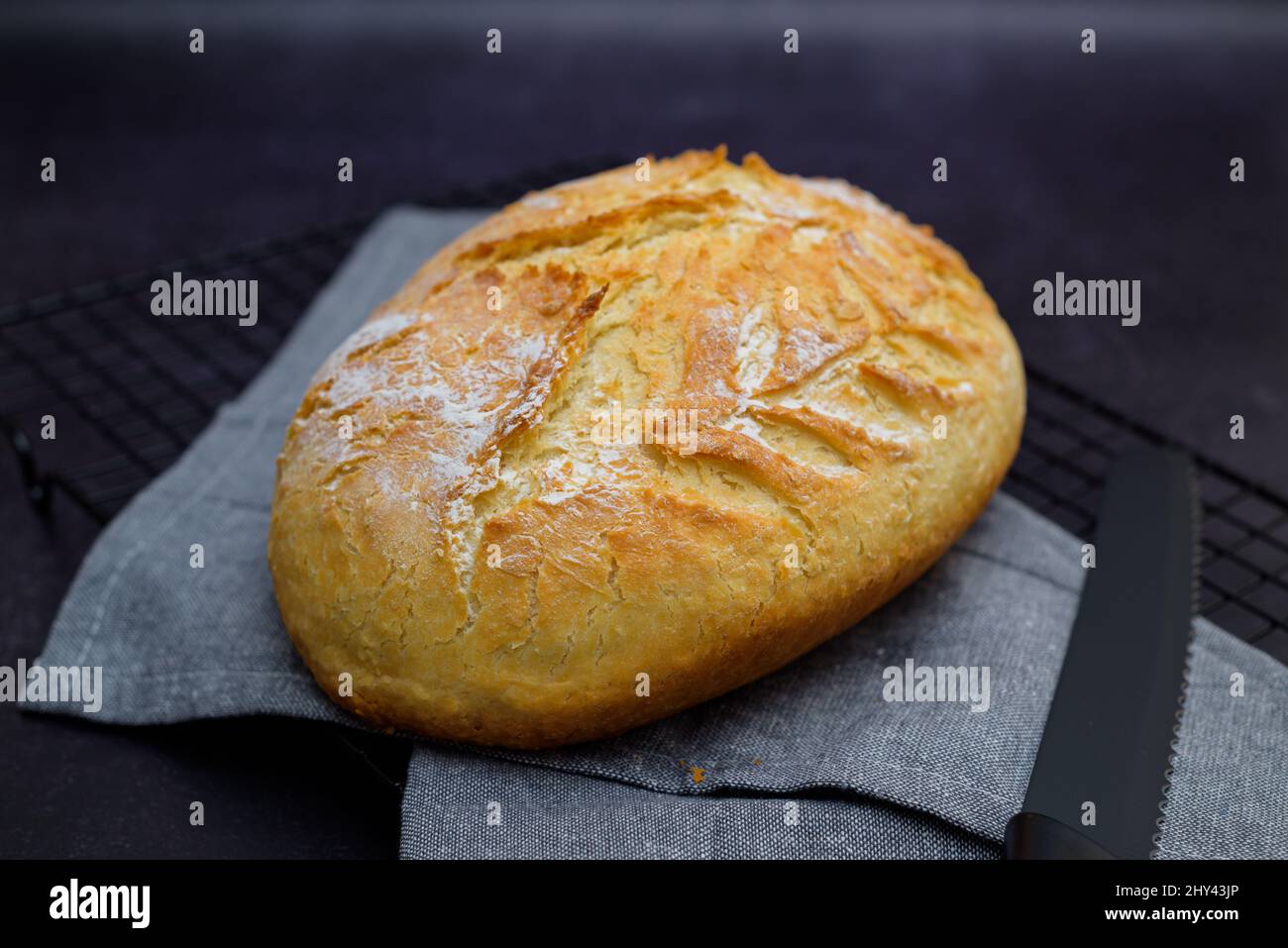 Loaf of sourdough bread and a knife on a cooling rack with a gray cloth ...