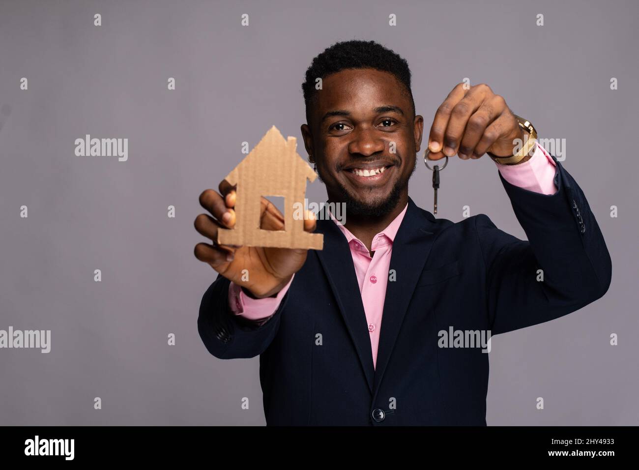 Young African real estate agent showing a cardboard house and a key ...