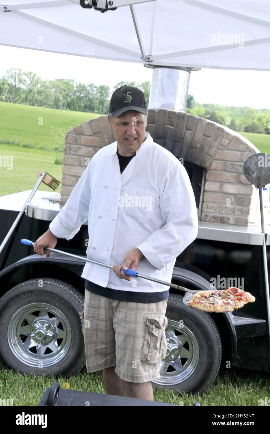 Cook prepares a pizza for baking in a wood-fired oven at an outdoor ...