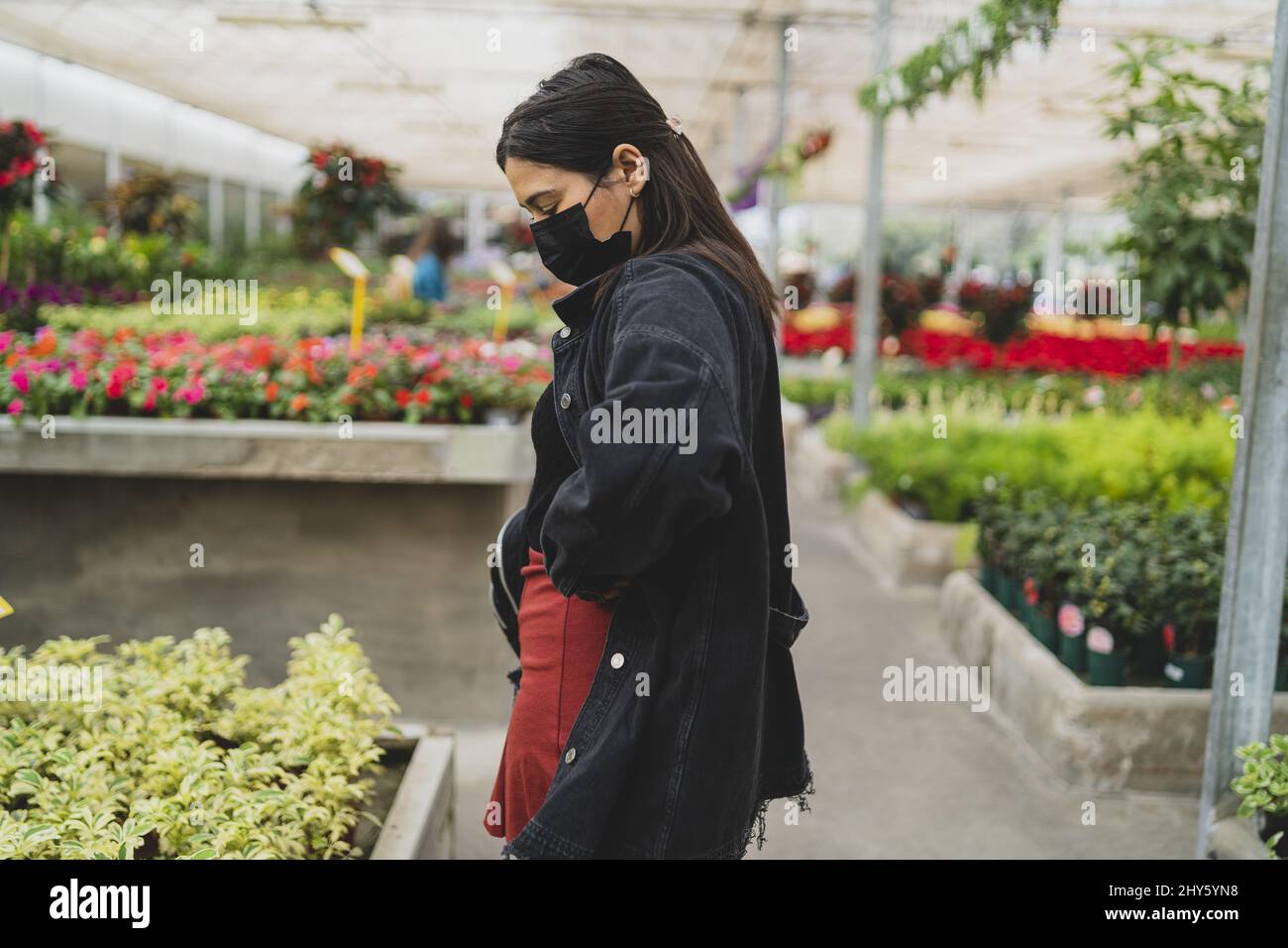 Caucasian young woman wearing a face mask looking at the exotic plants ...