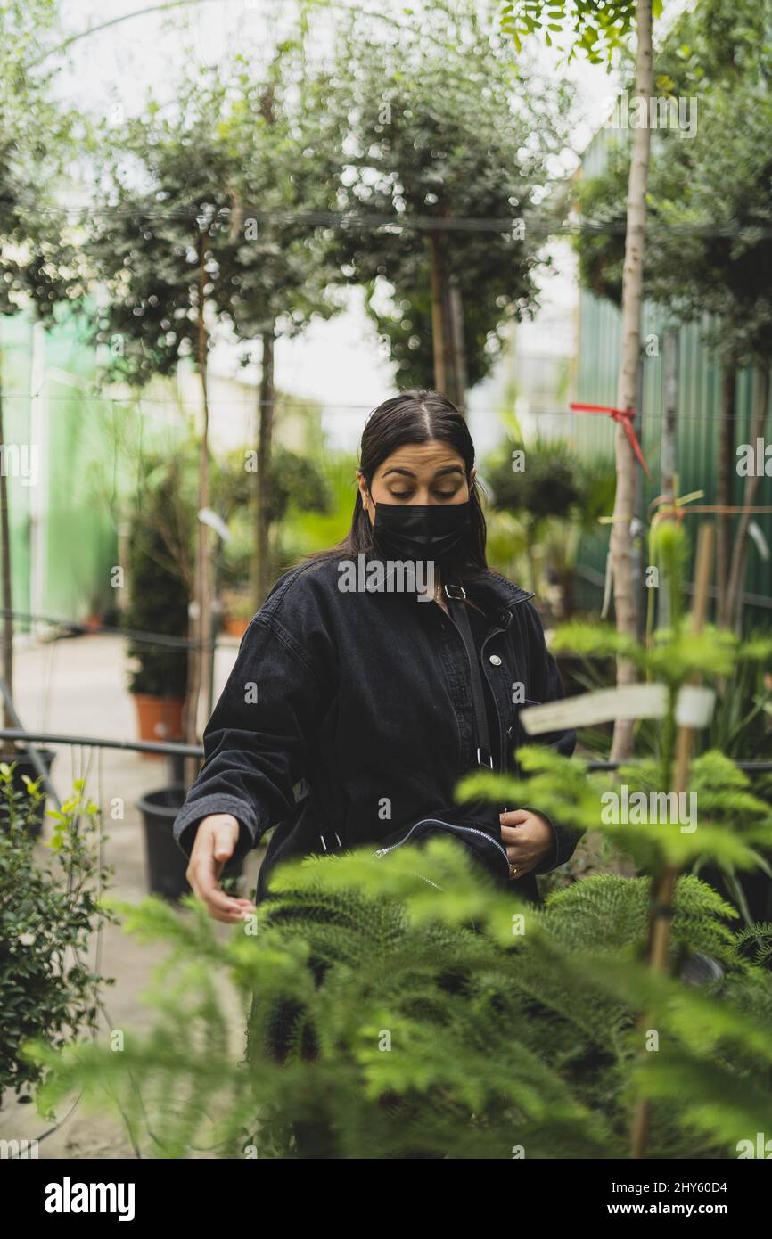 Caucasian young woman wearing a face mask looking at the exotic plants ...