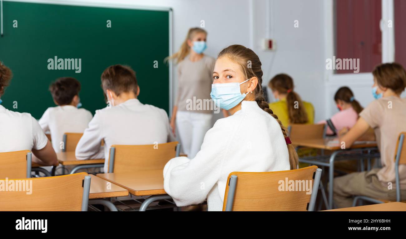 Student in protective mask studying in classroom, listening to lecturer ...