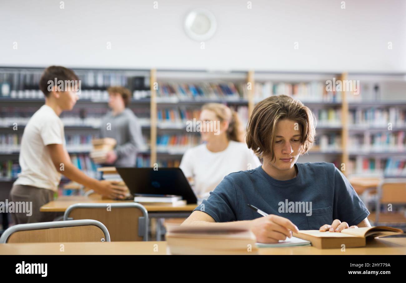 Teenager engaged in research working with books in library Stock Photo ...