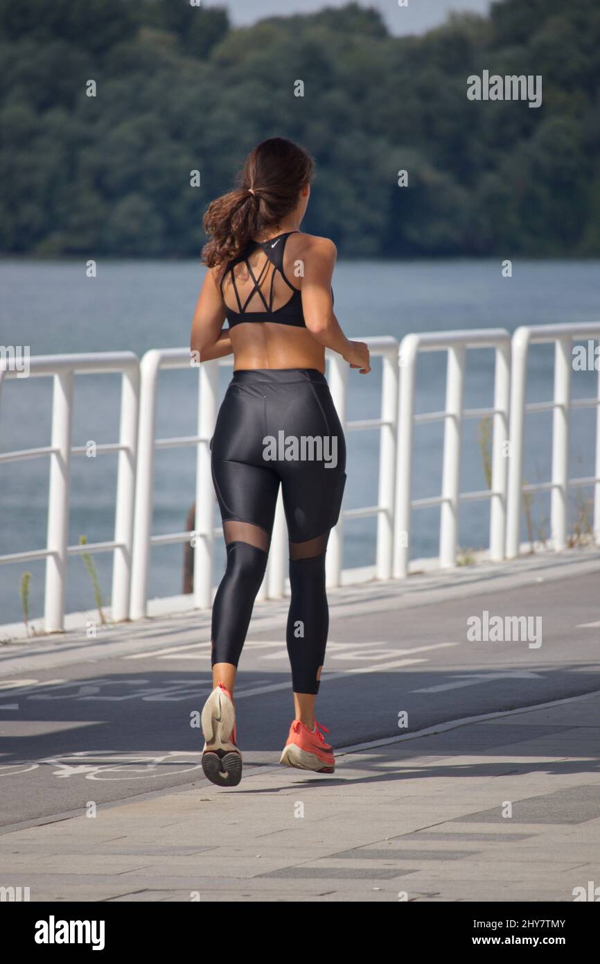 Vertical shot of a female from behind jogging on the track by the river ...