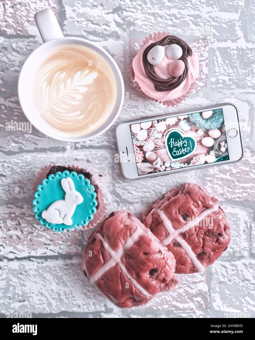 Vertical shot of smartphone, cup of coffee, hot cross buns and cupcakes ...
