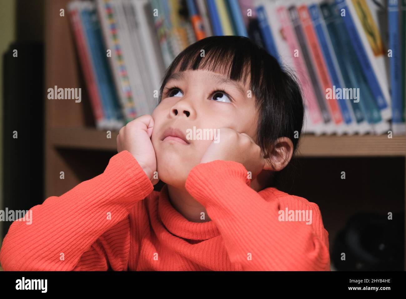 Portrait of cute child looking up and thinking with hands on chin in ...