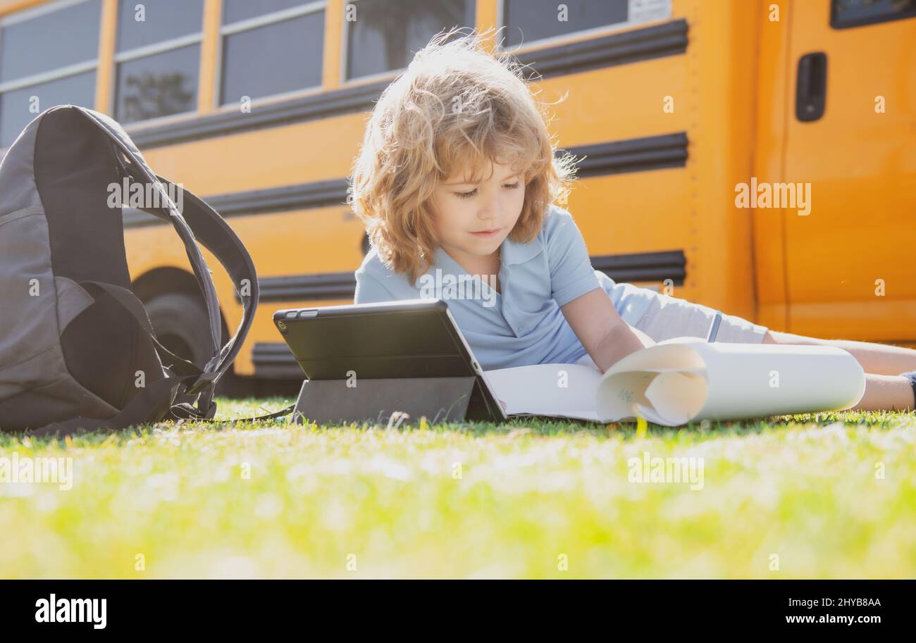 Cute schoolboy laying on grass in the park near school bus. School kid ...