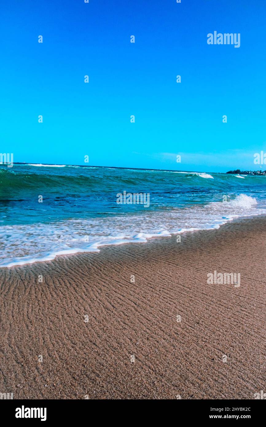 Vertical shot of the waves hitting the sandy shore on a hot summer day ...