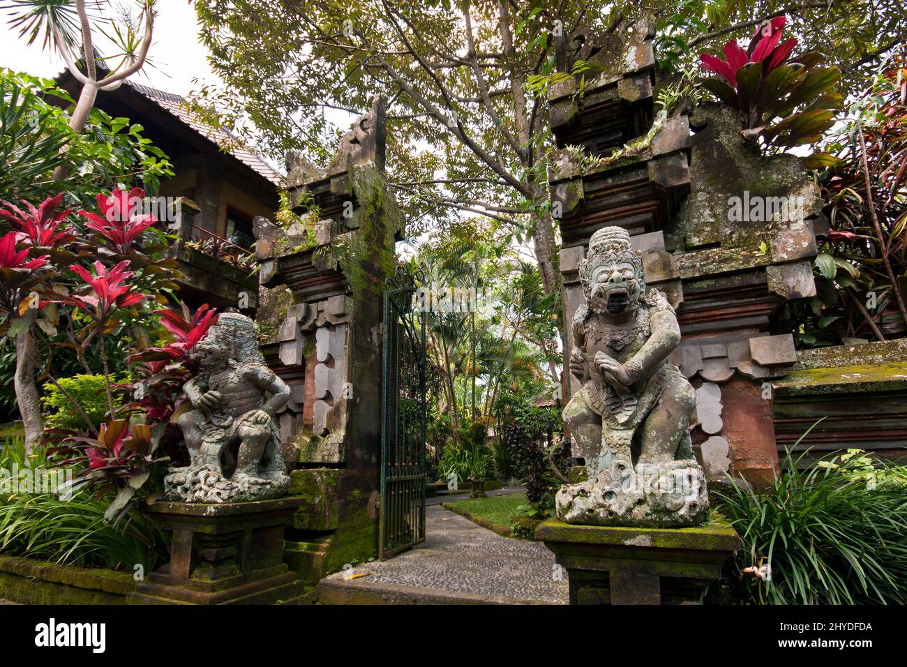Two old and weathered stone statues in front of a gate in Ubud, Bali ...
