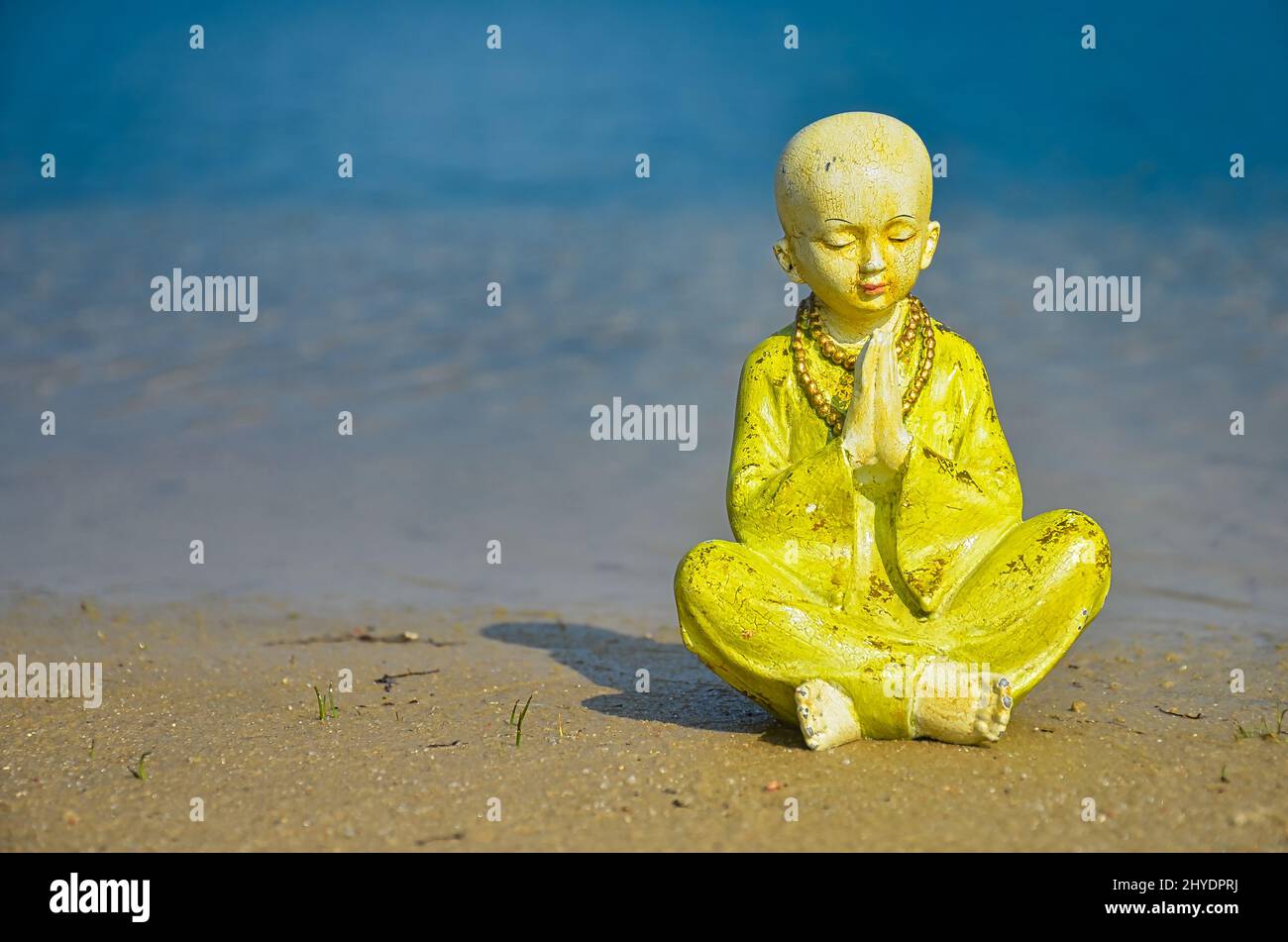 Closeup shot of a yellow Buddha figurine on the sand on the beach with ...