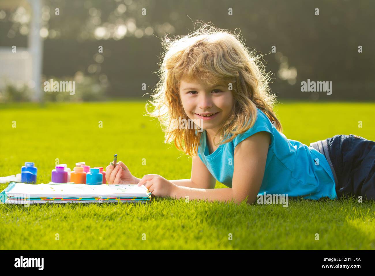 Child drawing. Kid draws in park laying in grass having fun on nature ...