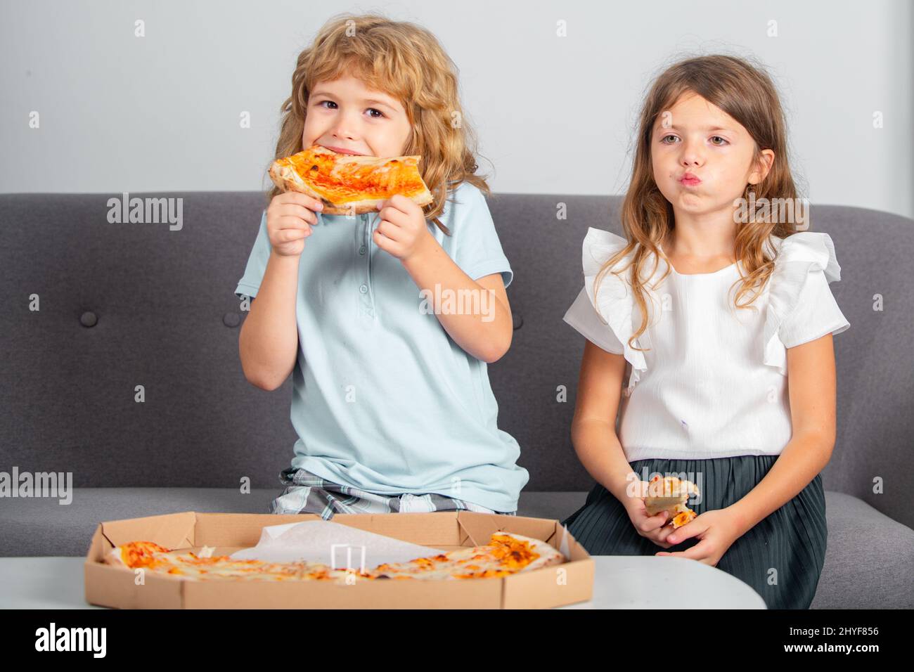 Children eating pizza. Two young children bite pizza indoors Stock ...