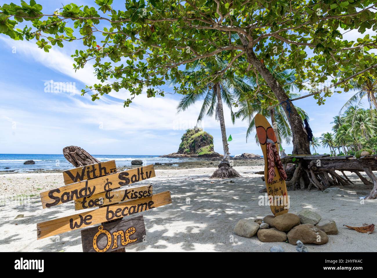 Wooden signboard on a beach next to some palms growing in the sunny day ...