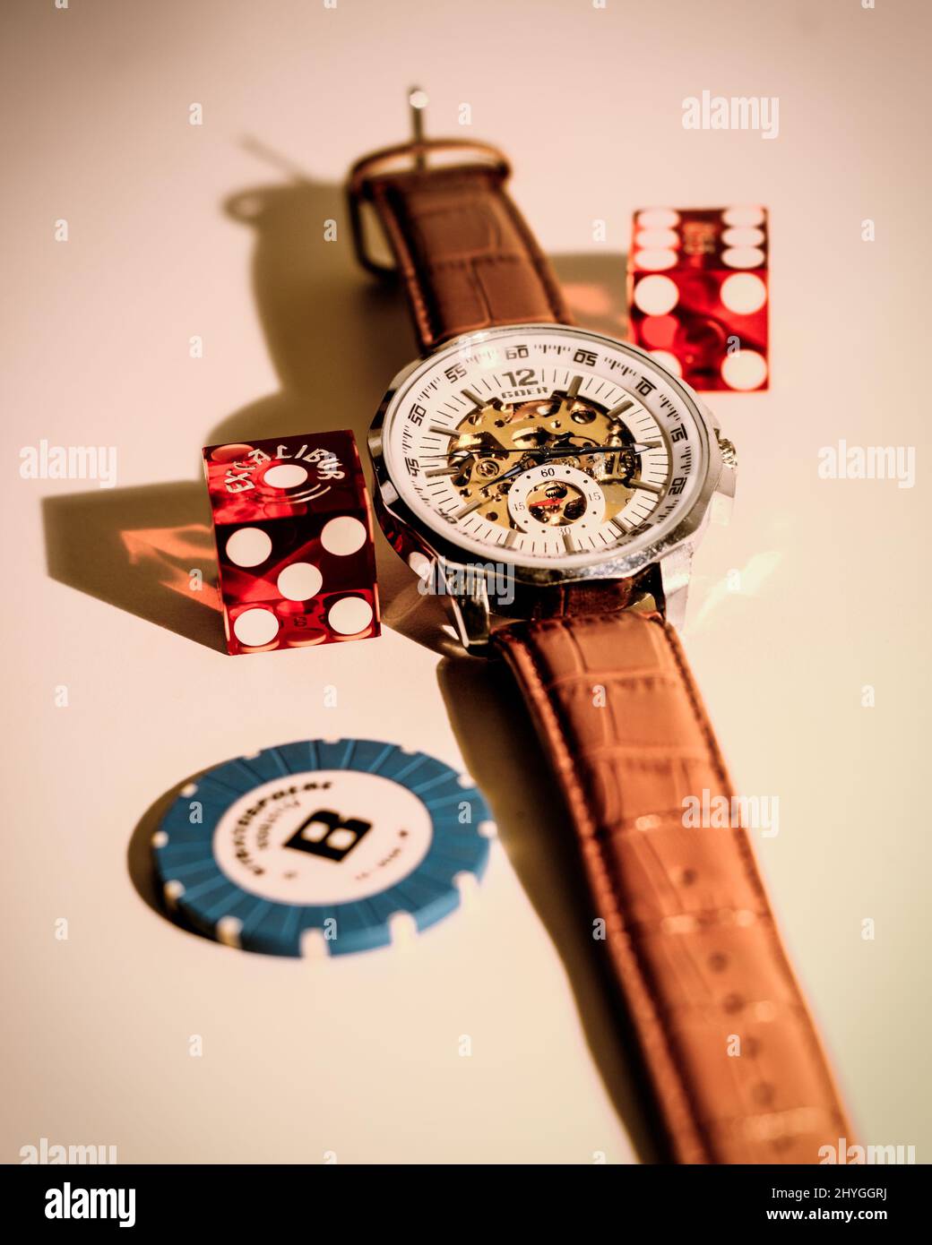 Vertical shot of a wrist watch with dice and a poker chip on a white ...