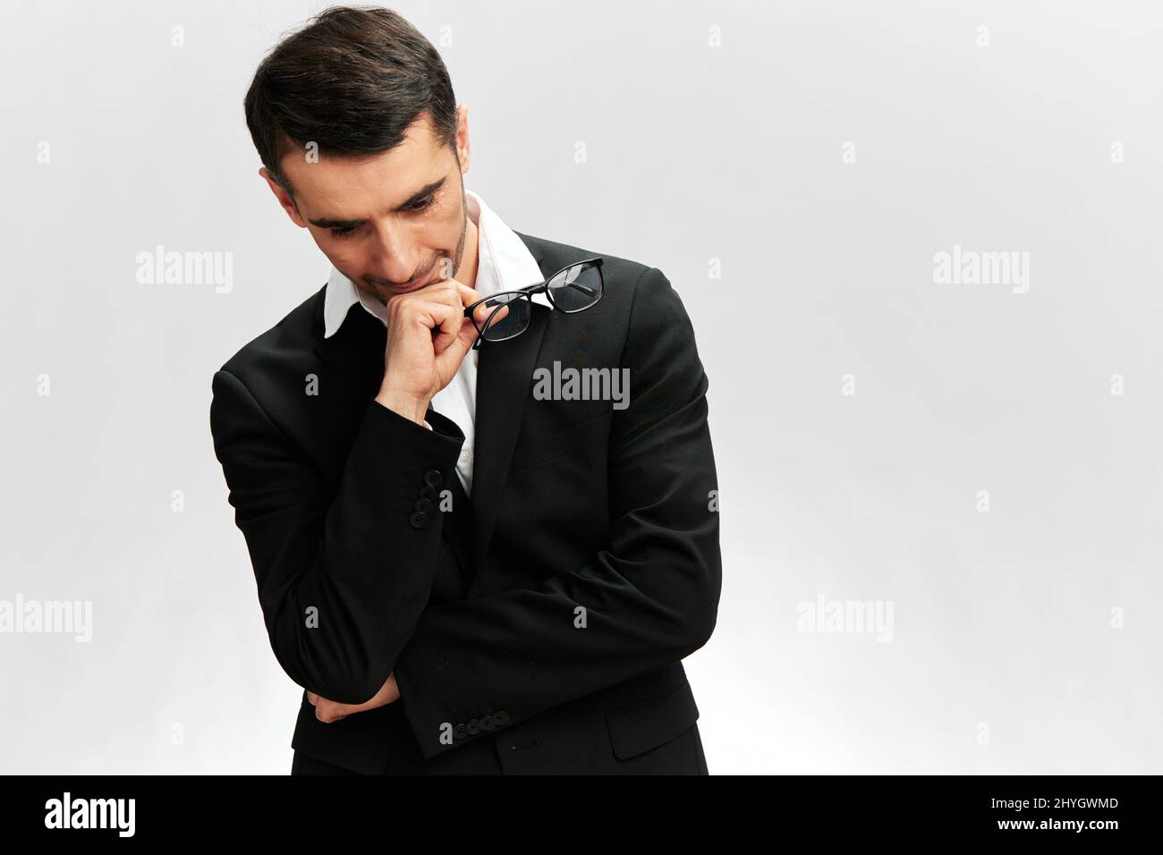 a man in a black business suit with a pensive look looks down glasses ...