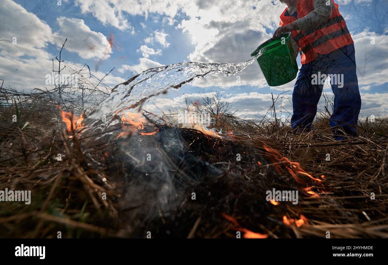 Fireman ecologist extinguishing wildfire in field with cloudy sky on ...