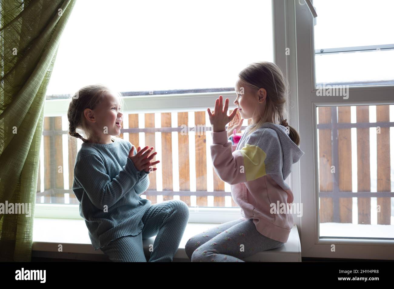 two girls are playing patty-cake, sitting on the windowsill near the ...