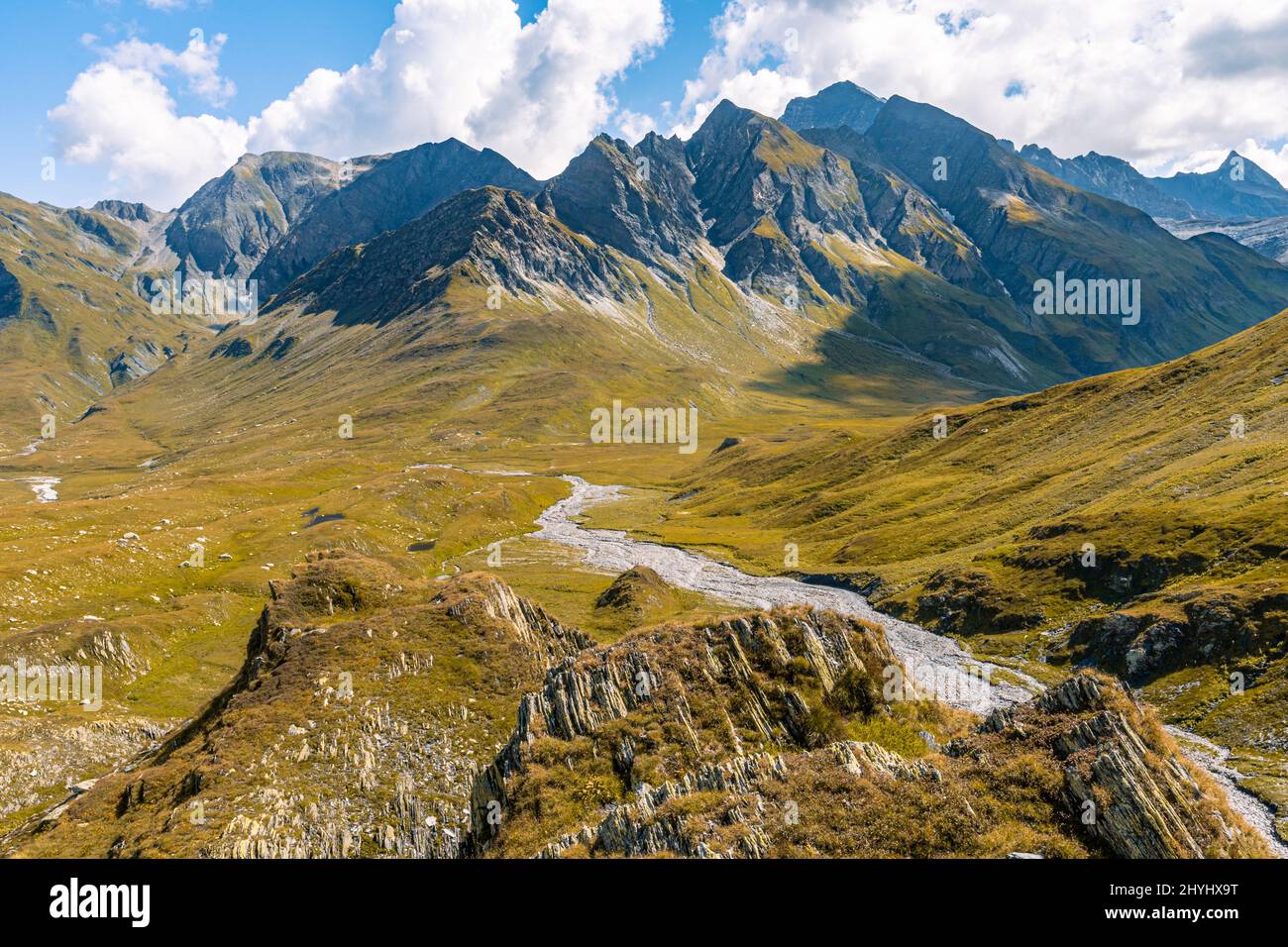 Alpine landscape with a grassy expanse and a dry, rocky river bed ...