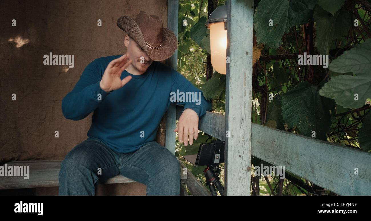 Cowboy man communicates online using his phone while sitting on porch ...