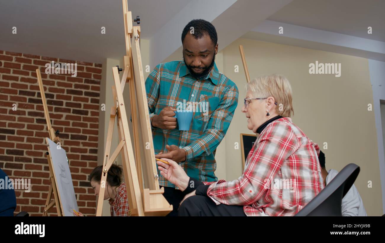 African american teacher guiding senior woman to draw sketch on canvas ...