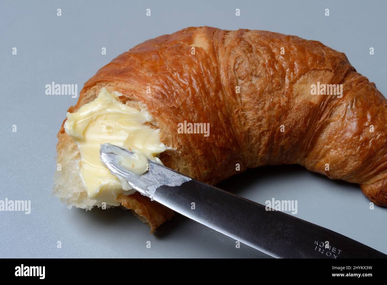 Butter with knife on croissant Stock Photo - Alamy
