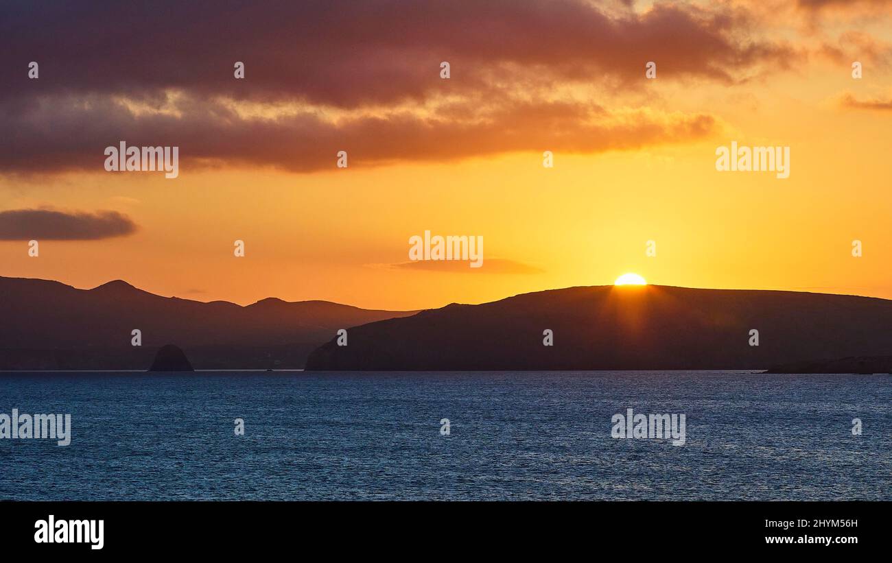 Sunset, sun going down behind hill, mountains in background, sky orange ...