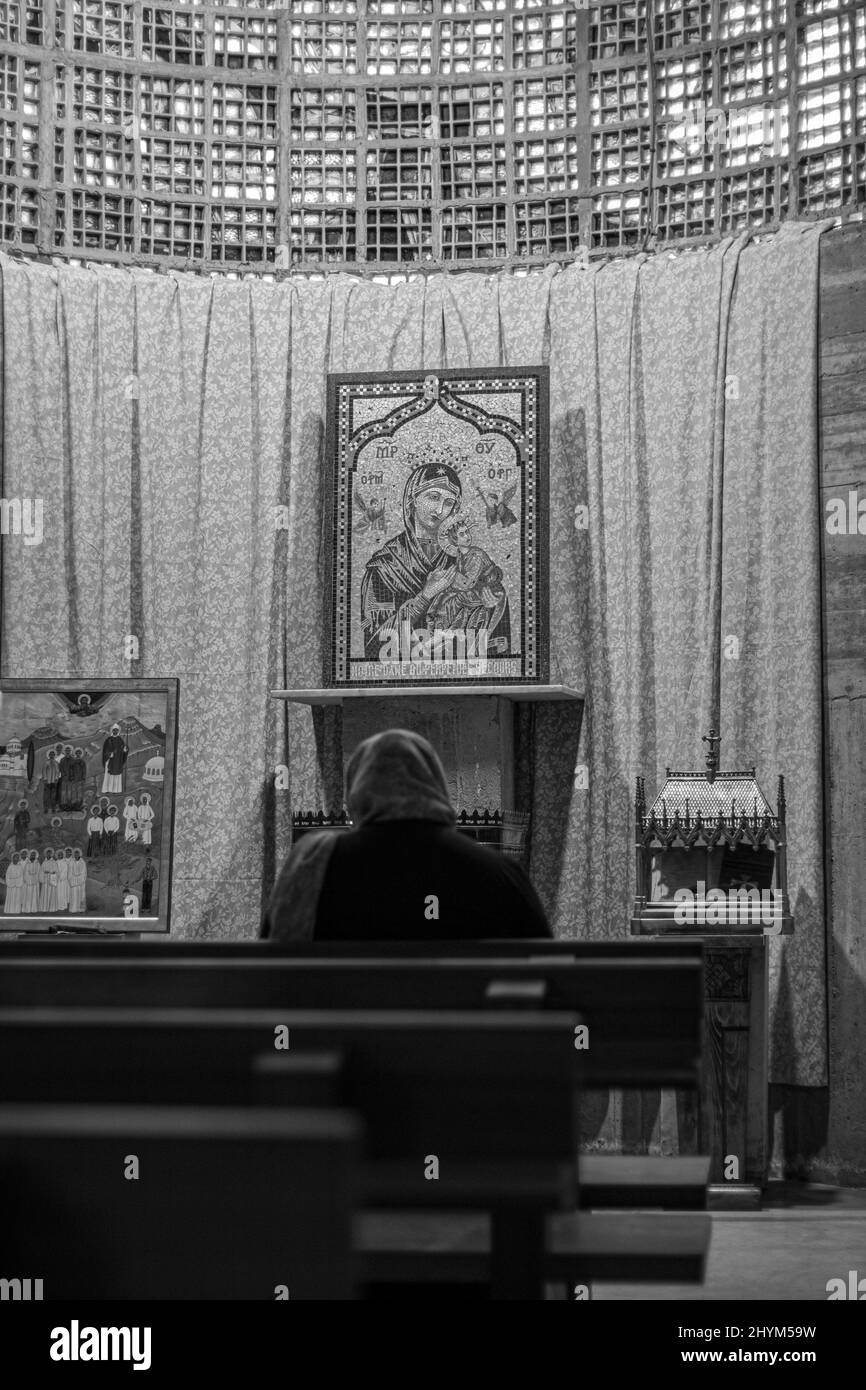 Vertical grayscale shot of the woman praying in front of icon in church ...