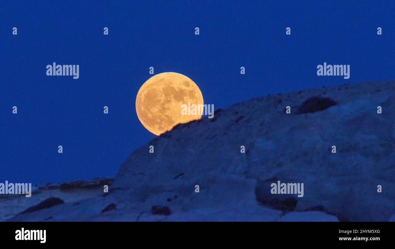 Telephoto shot, Large yellow full moon over rocks, sky midnight blue ...