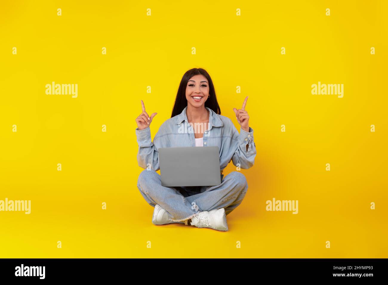 Happy lady using laptop pointing up at studio Stock Photo - Alamy