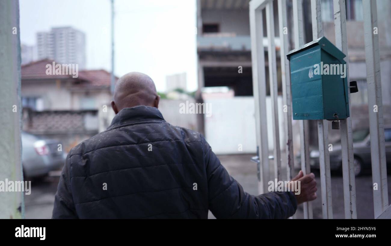 An older man leaving house in the drizzle opening entrance door and ...