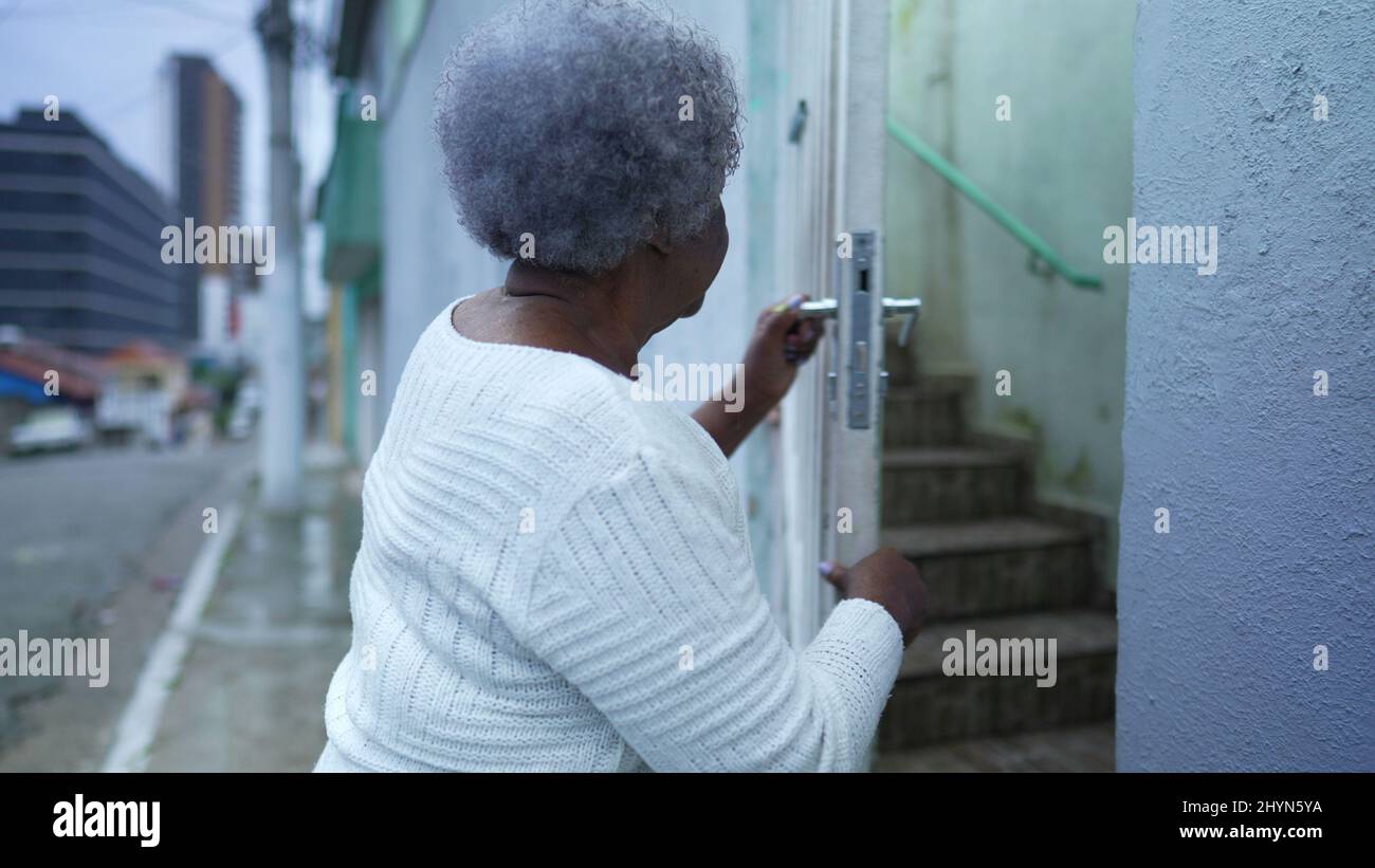 An older woman arriving home opening front gate and entering house ...