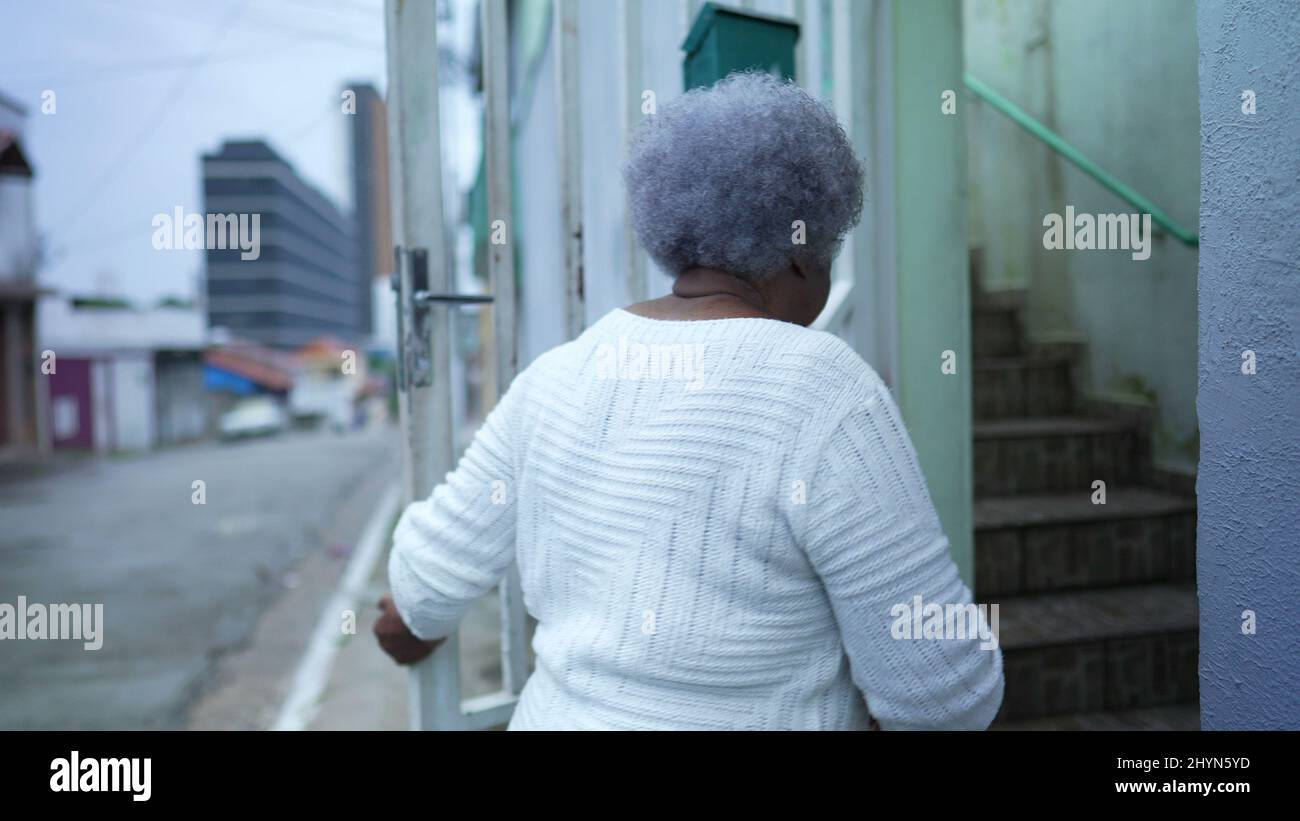 An older woman arriving home opening front gate and entering house ...