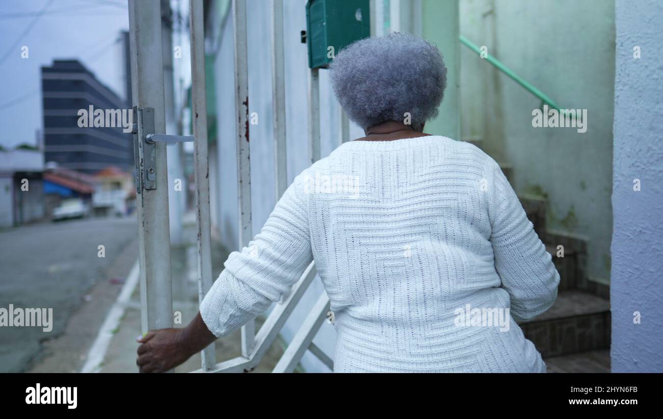 An older woman arriving home opening front gate and entering house ...