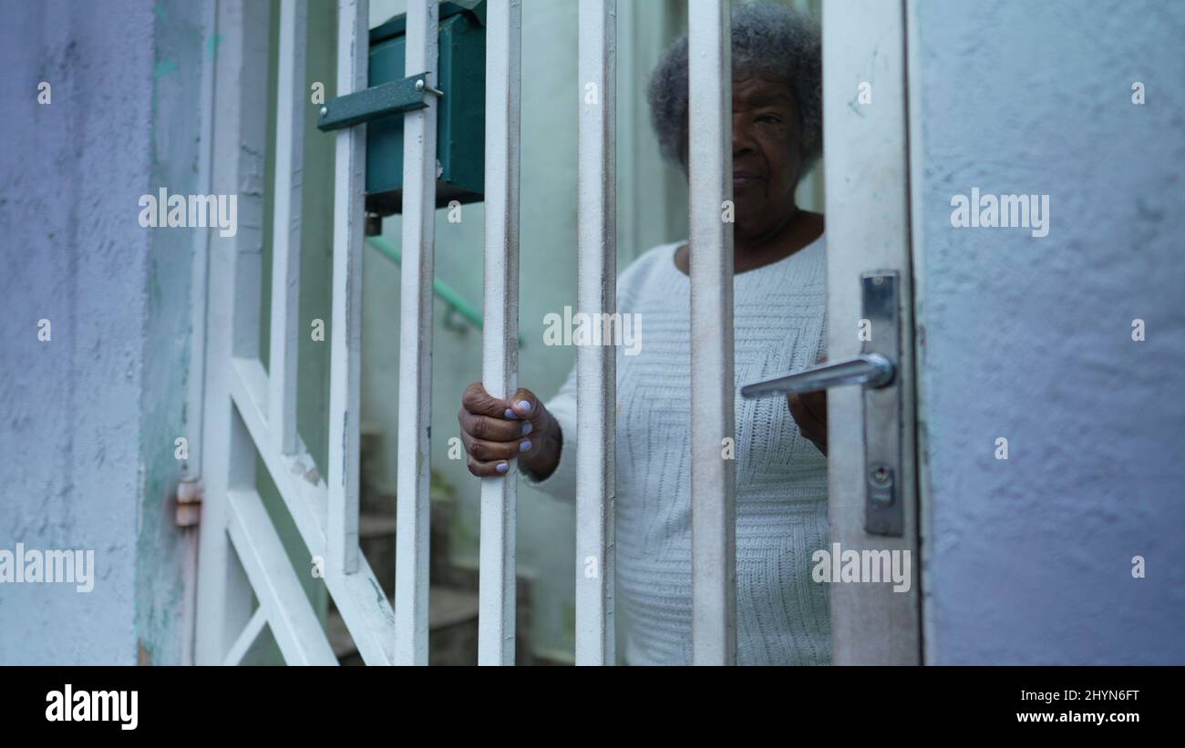An older woman arriving home opening front gate and entering house ...