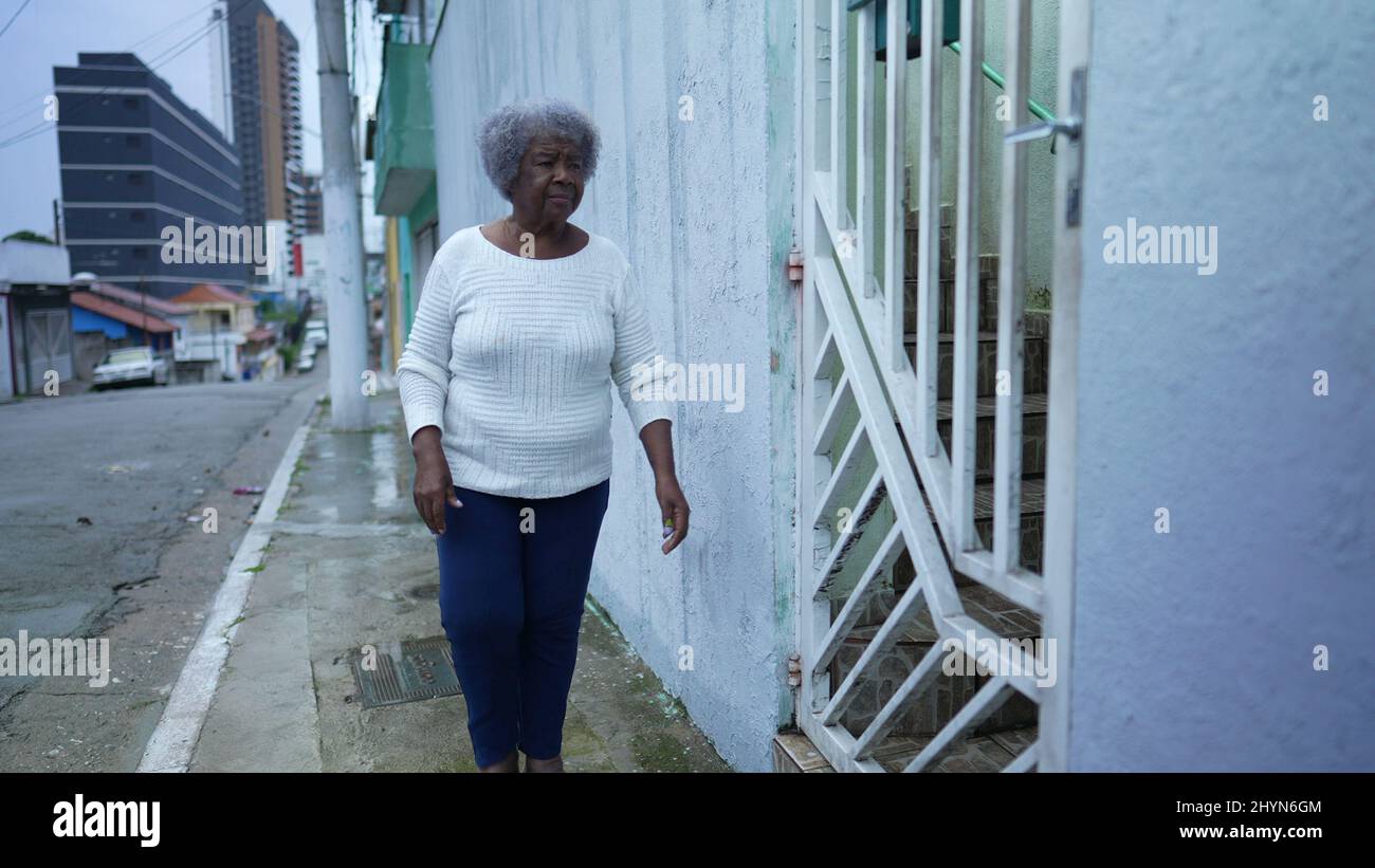 An older woman arriving home opening front gate and entering house ...