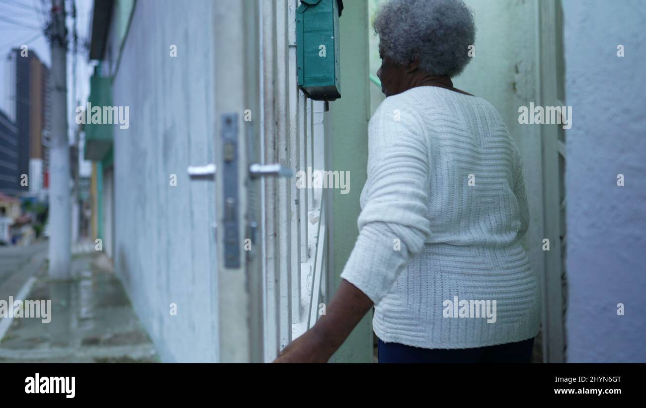 An older woman arriving home opening front gate and entering house ...