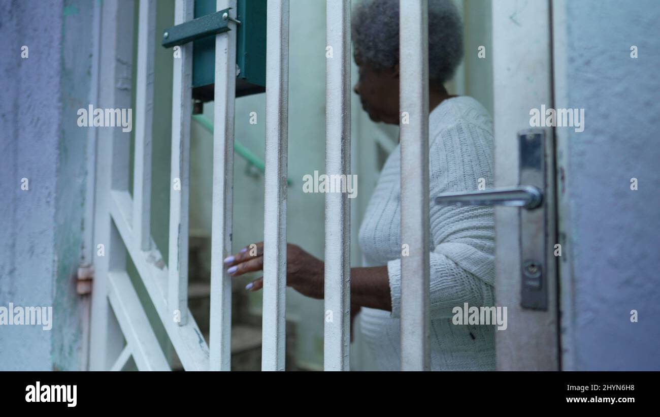 An older woman arriving home opening front gate and entering house ...