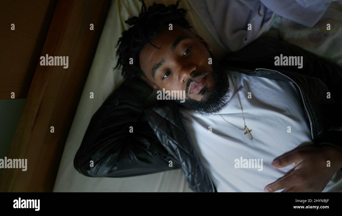 A pensive black man lying down in bed a resting young African man ...