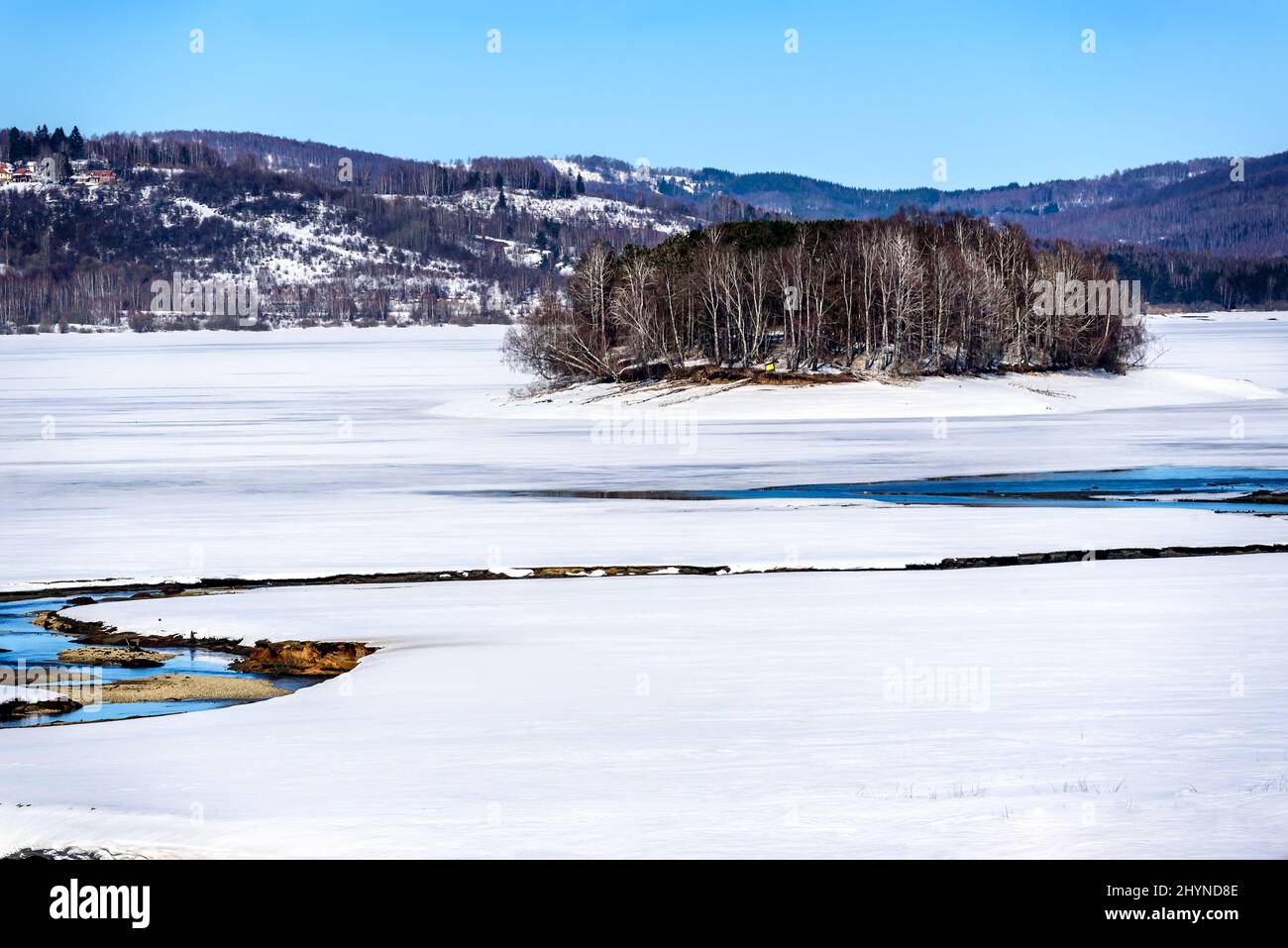 Winter landscape with a tributary River entering the frozen lake with ...