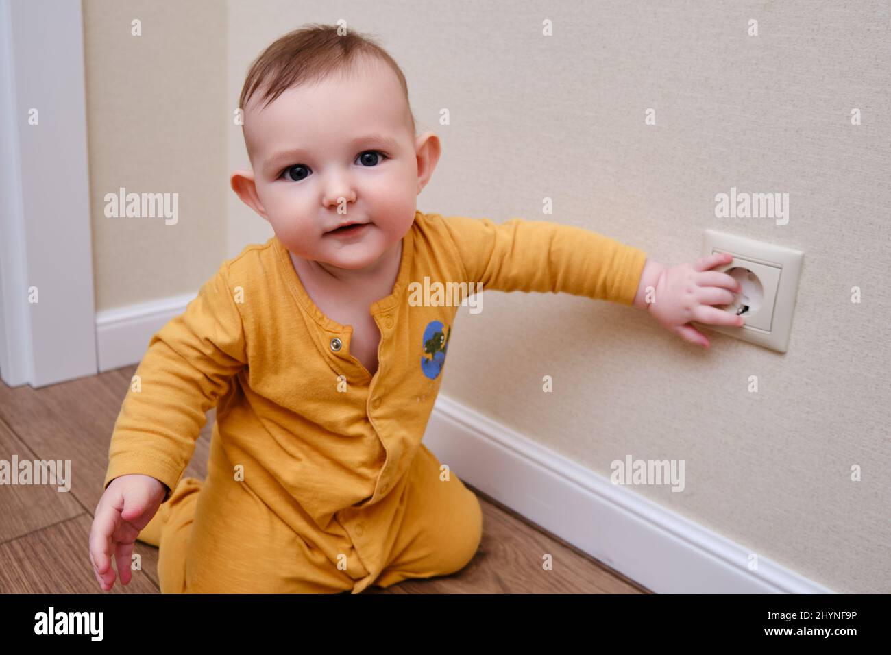 Baby toddler reaches into the electrical outlet on the home wall with ...