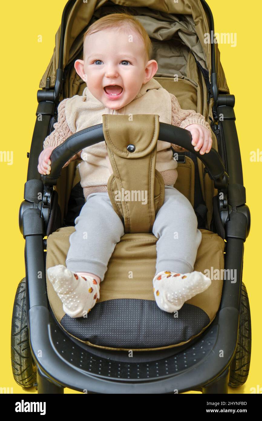 A happy child is sitting in a baby carriage on a studio yellow ...