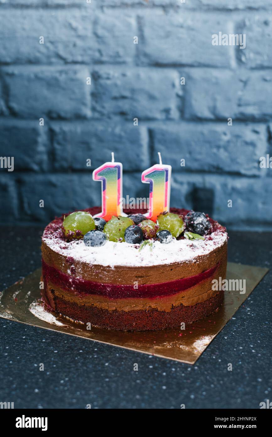 A festive fruit cake with candles with numbers 11 on a blue table Stock ...