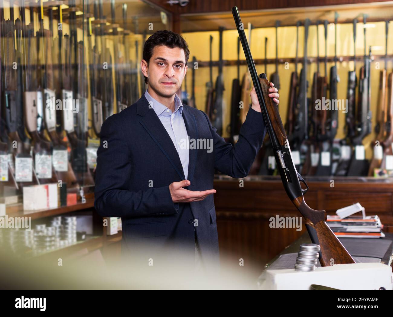 Portrait of positive male seller in gun shop showing shotgun Stock ...