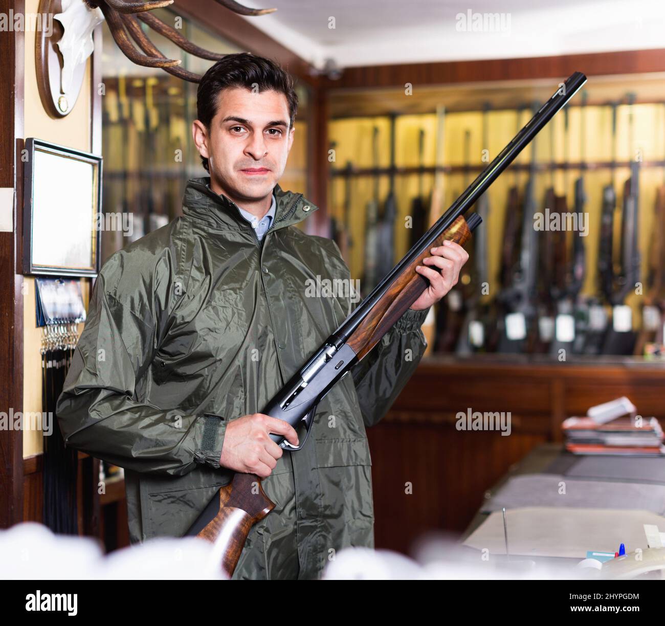 Cheerful hunter male wearing windbreaker in hunting shop with rifle in ...