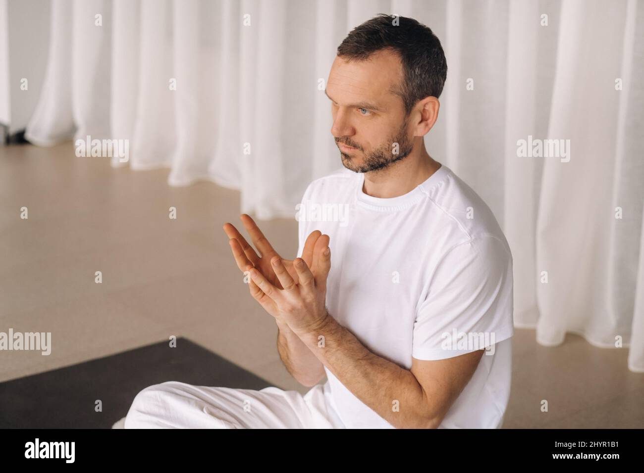 a man in white sportswear is doing yoga with a fitness room. the ...