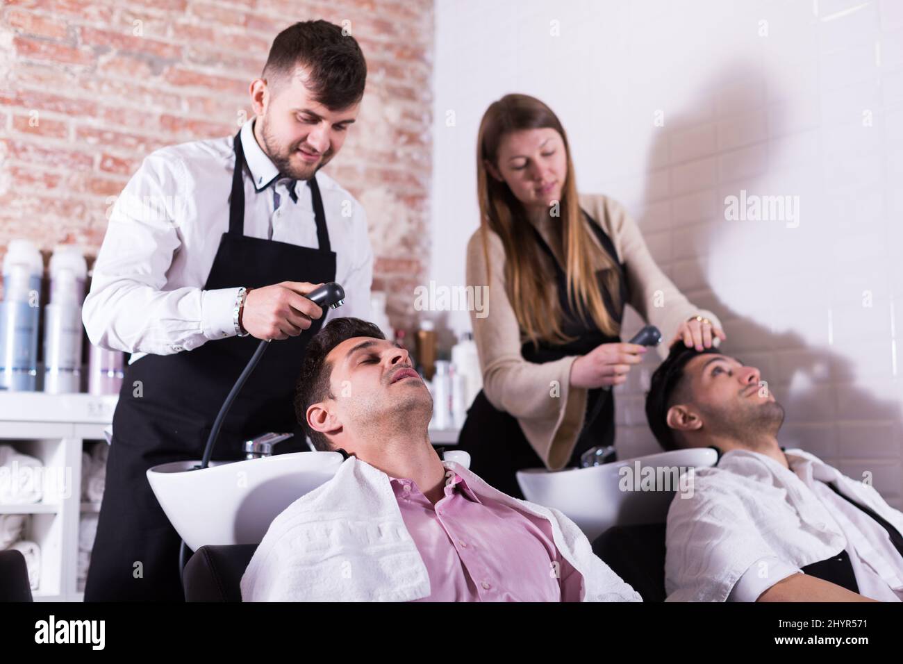 Man and woman hairdressers washing hair of male clients of modern hair ...